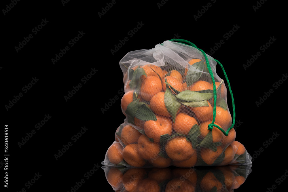 Tangerines in a reusable mesh bag. Isolated black background with copy ...