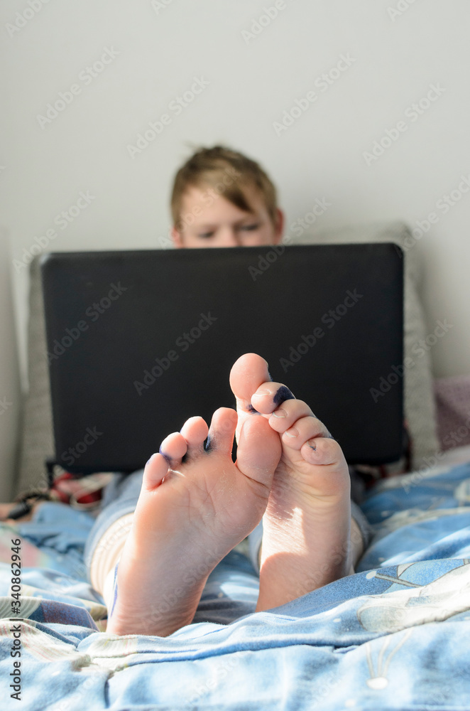 Bare feet, distance learning during quarantine, a boy sitting on a sofa ...