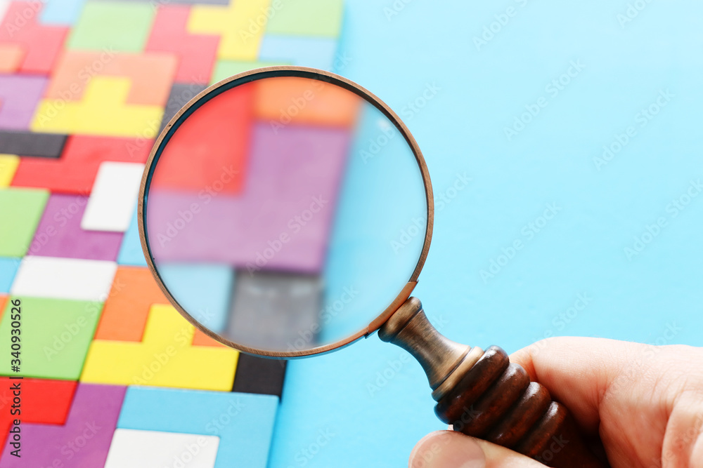 concept image of magnifying glass over puzzle background. finding the ...