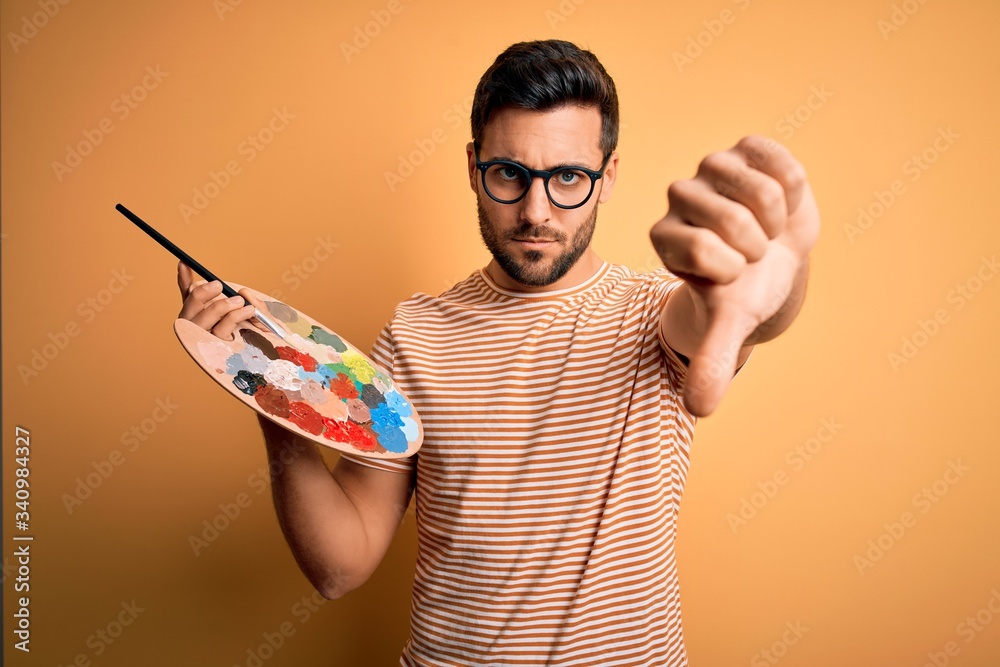 Young handsome artist man with beard painting using bursh and palette ...