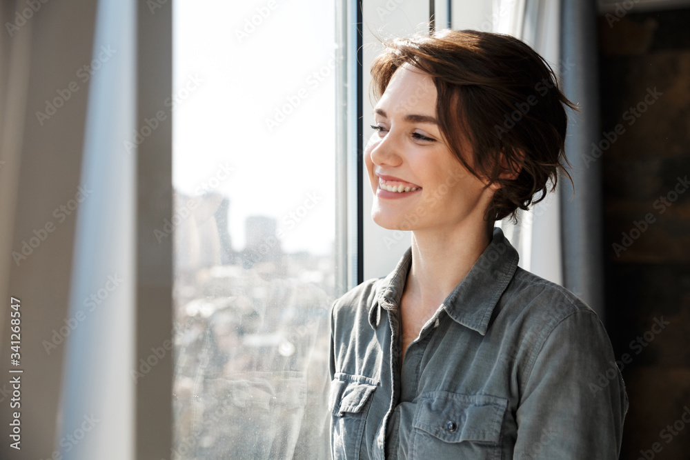 Image of beautiful young joyful woman smiling and looking at window ...