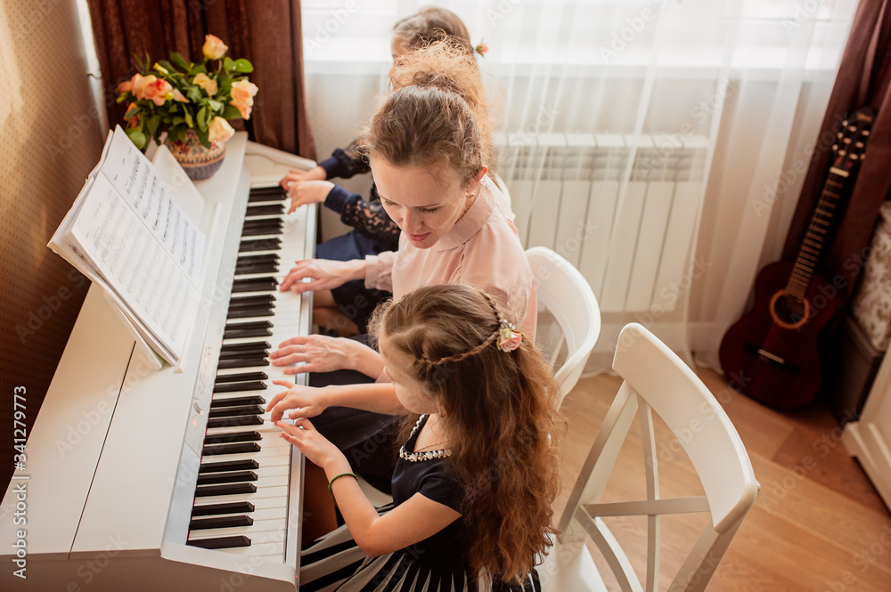 Home piano lesson. A woman and two girls practice sheet music on one ...