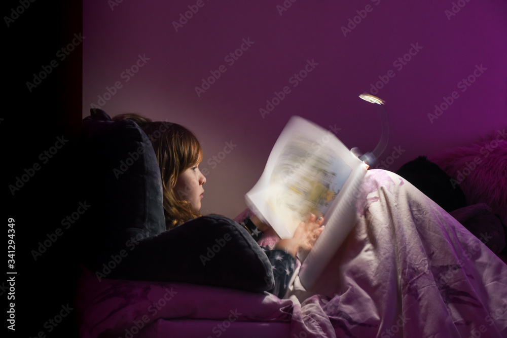 Girl reading a book in bed at night in comfy bedroom wearing pyjamas ...