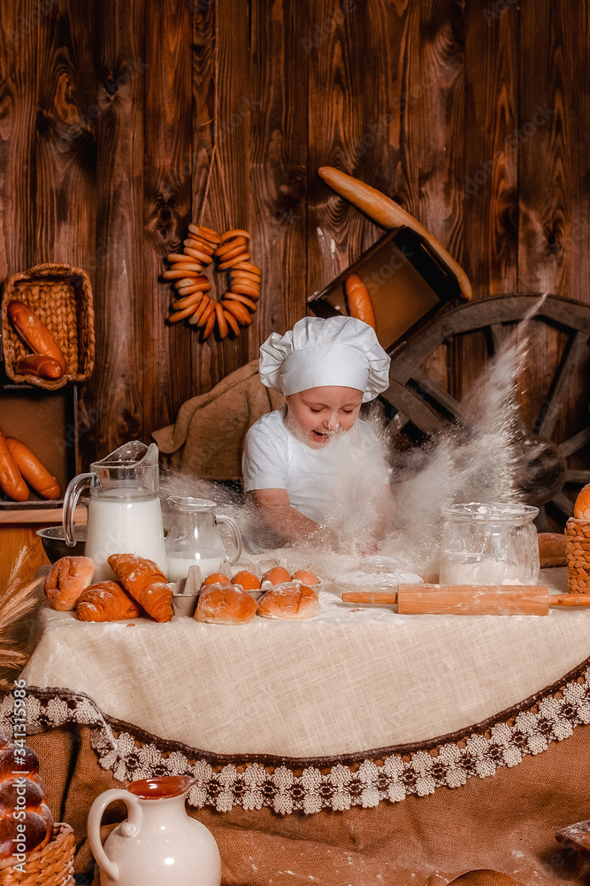 Little kid in a chef's hat playing role of baker and knead bread dough. Table is full of mess ...