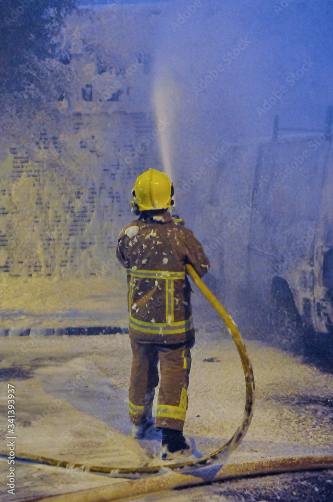 Fireman sprays foam onto a shop to prevent fire from spreading from a ...
