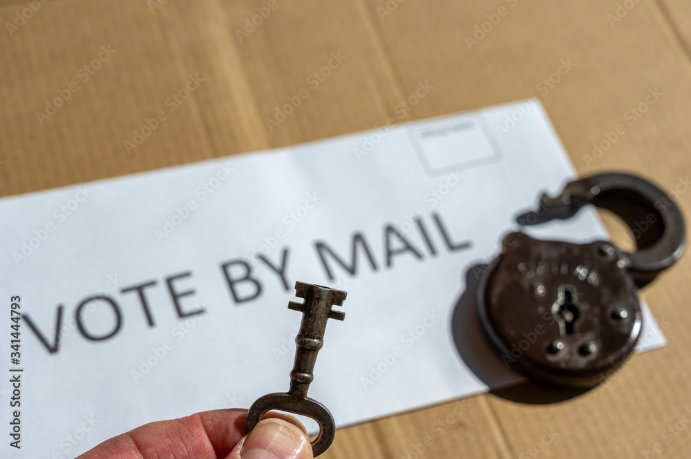 Hand holding a key in front of envelope for vote by mail ballot ...