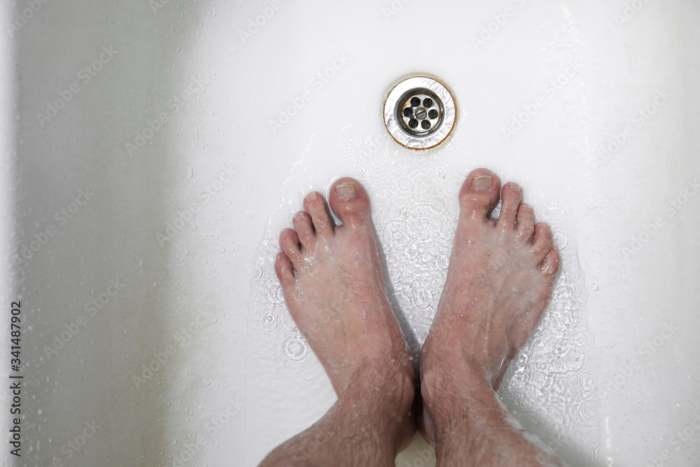 Feet standing under shower, drain on floor, flowing water in bathroom ...
