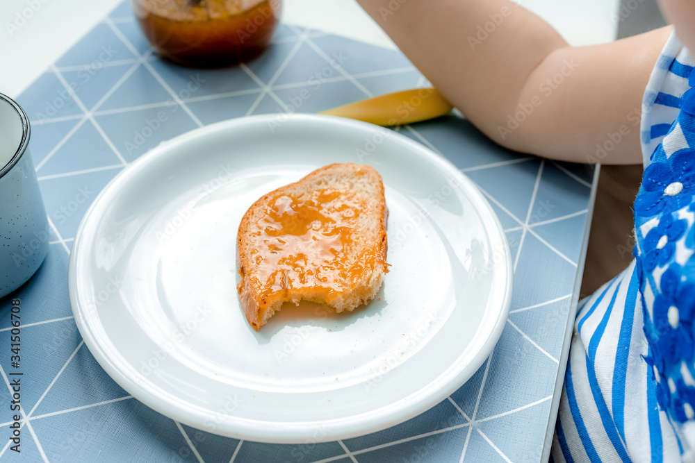 Eating a slice of bread and jam. Little girl eating jam at table in ...