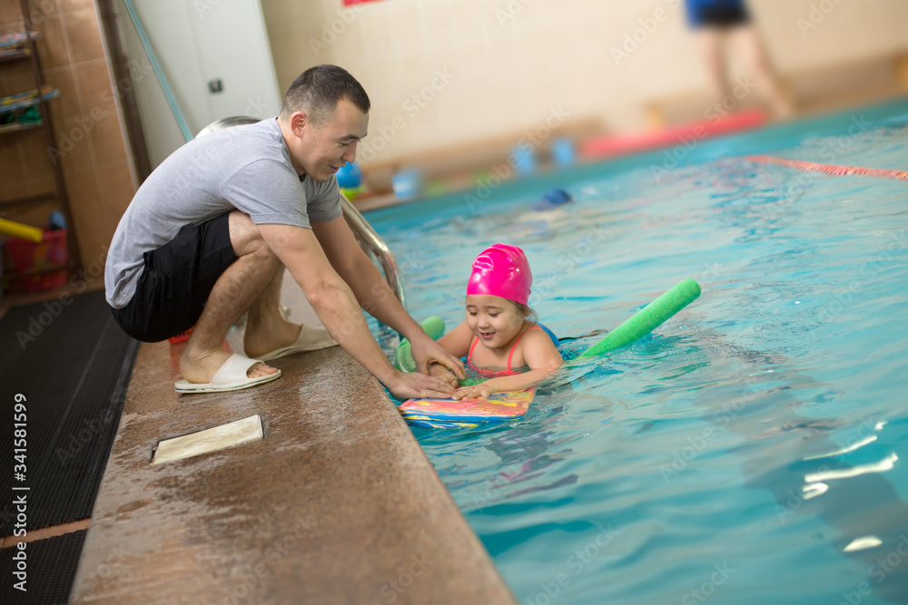 Pretty little girl learning to swim in the pool with swim coach trainer ...