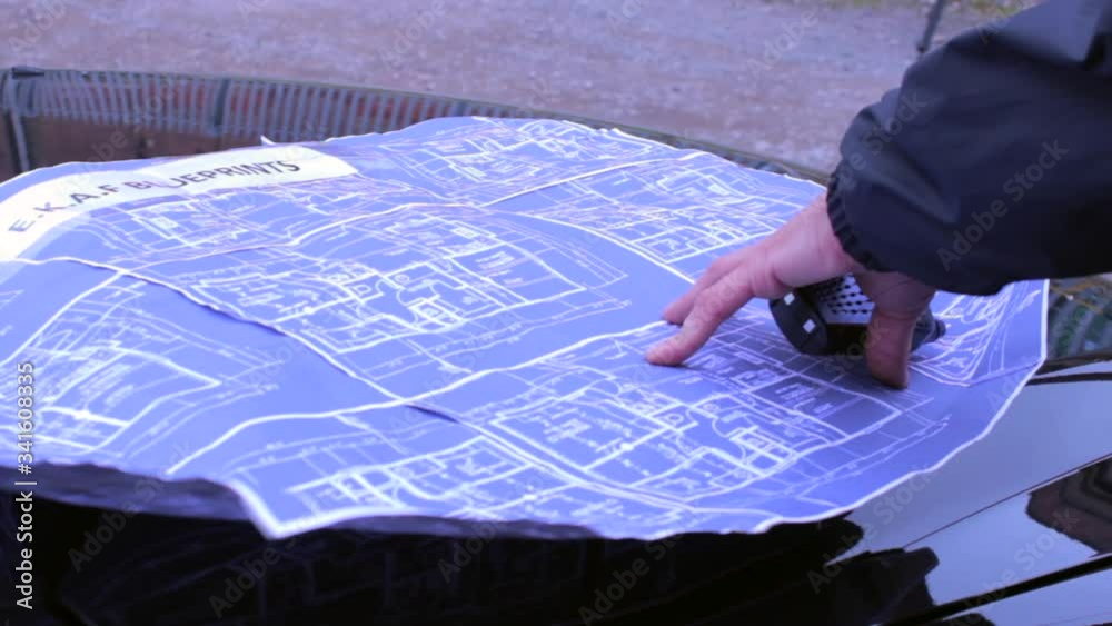 Man planning entry into building using blueprints on car hood. The man ...