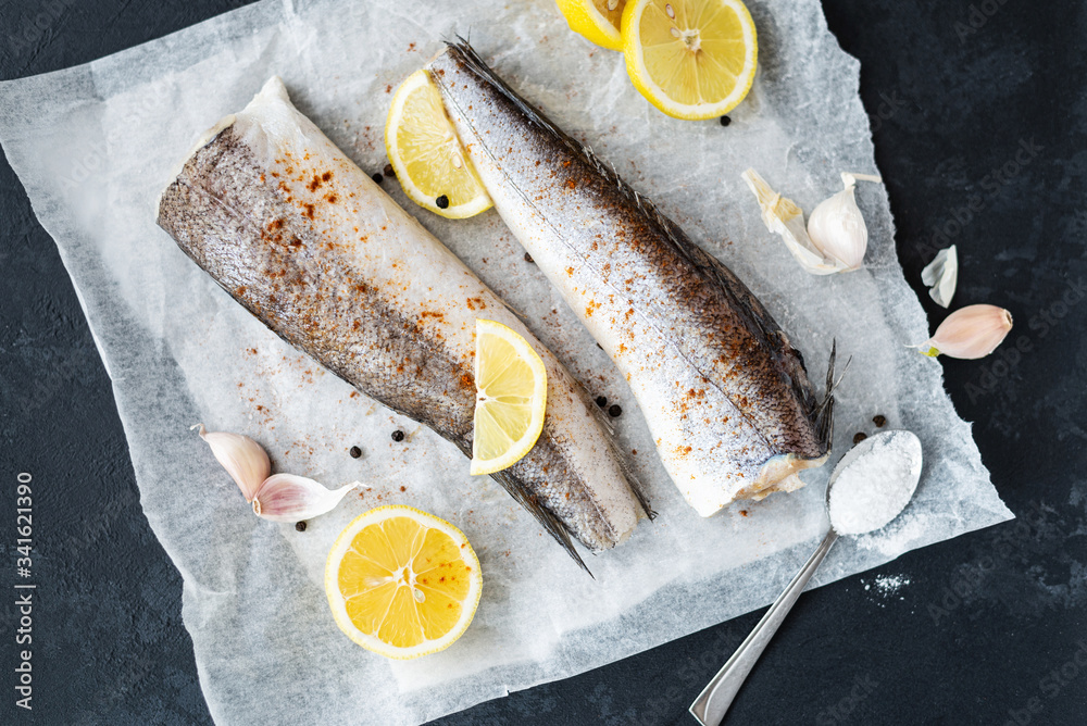 Fresh raw hake fillet on a black background. Fresh fish with lemon ...