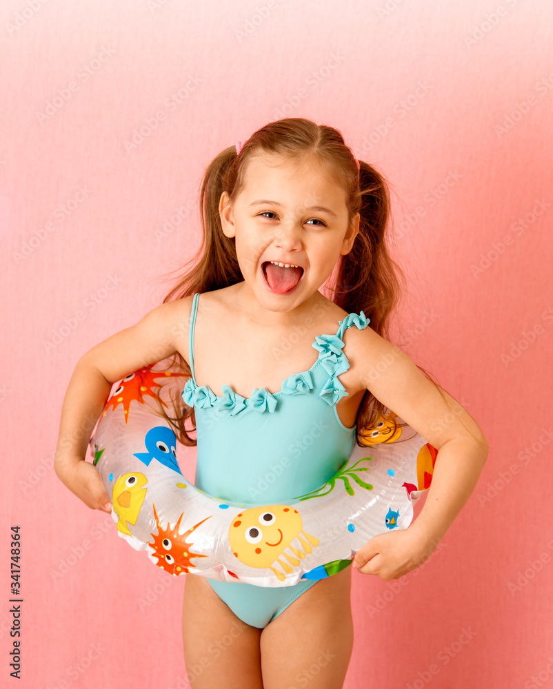 little girl in a swimsuit and with a rubber ring on a pink background ...