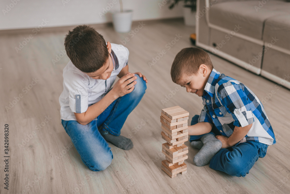 Two brothers boys build a tower of wooden blocks of the house on the ...