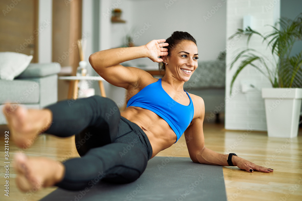 Happy muscular build woman doing side sit-ups while exercising at home ...