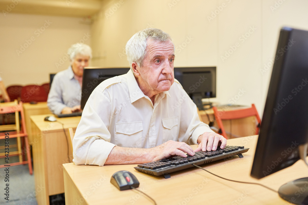 Senior Mann sitzt am PC in einem Computerkurs der VHS oder im ...