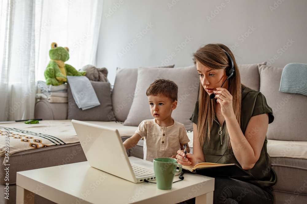 Mother working on laptop at home, while her child. Boy and mother using ...