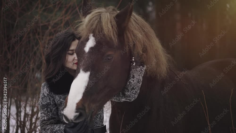 A young brunette cowgirl taking care of mare riding horse while winter ...