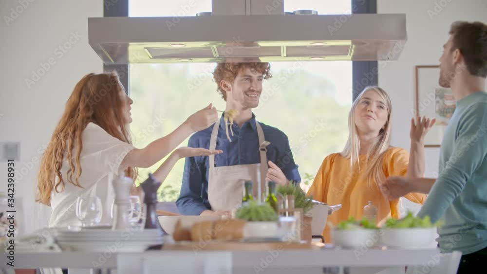 Four people talking while cooking together at home in modern kitchen ...