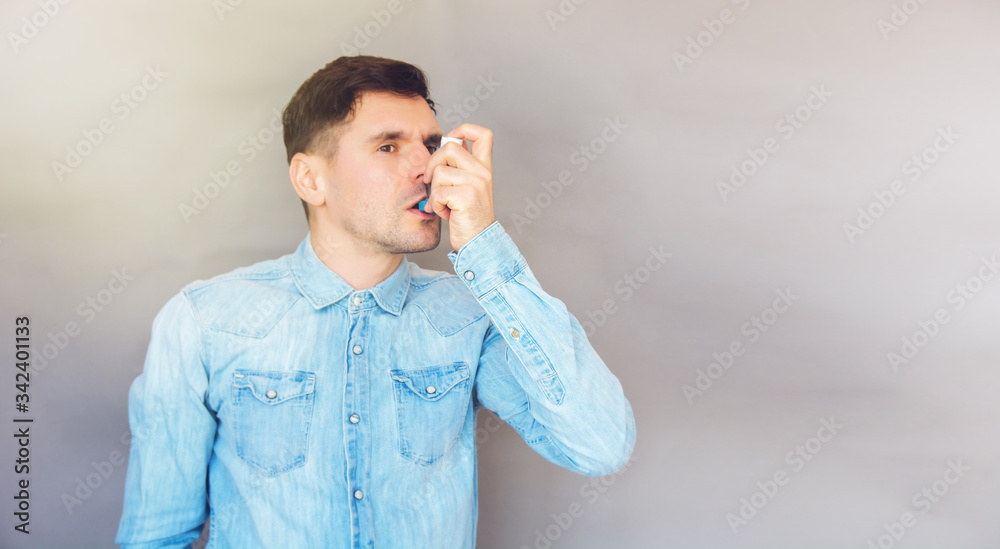 Young man using blue asthma inhaler during asthmatic attack to prevent ...