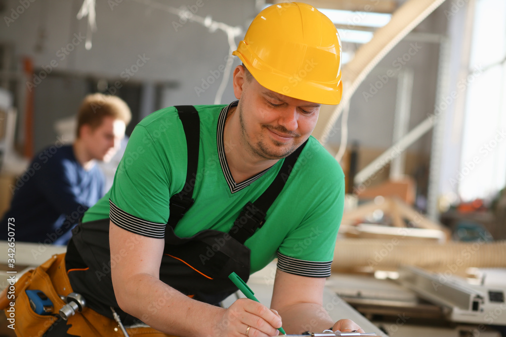 Portrait of young attractive man in work clothes and yellow helmet ...