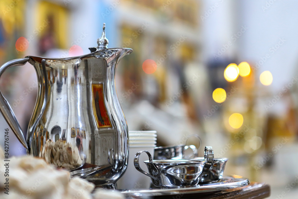 A metal jug with a cross on top and cups of water are used for drinking ...