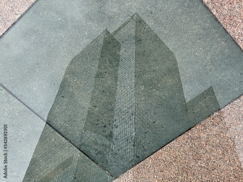 Inverted reflection of skyscraper and clouds in a puddle on sidewalk ...