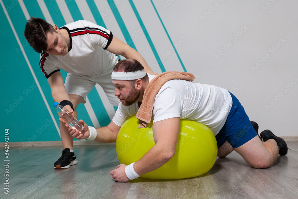 Overweight man is lying on the fitness ball in the gym while his ...