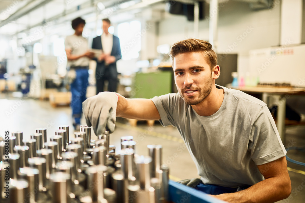 Happy manual worker examining manufactured rod cylinders in a factory ...
