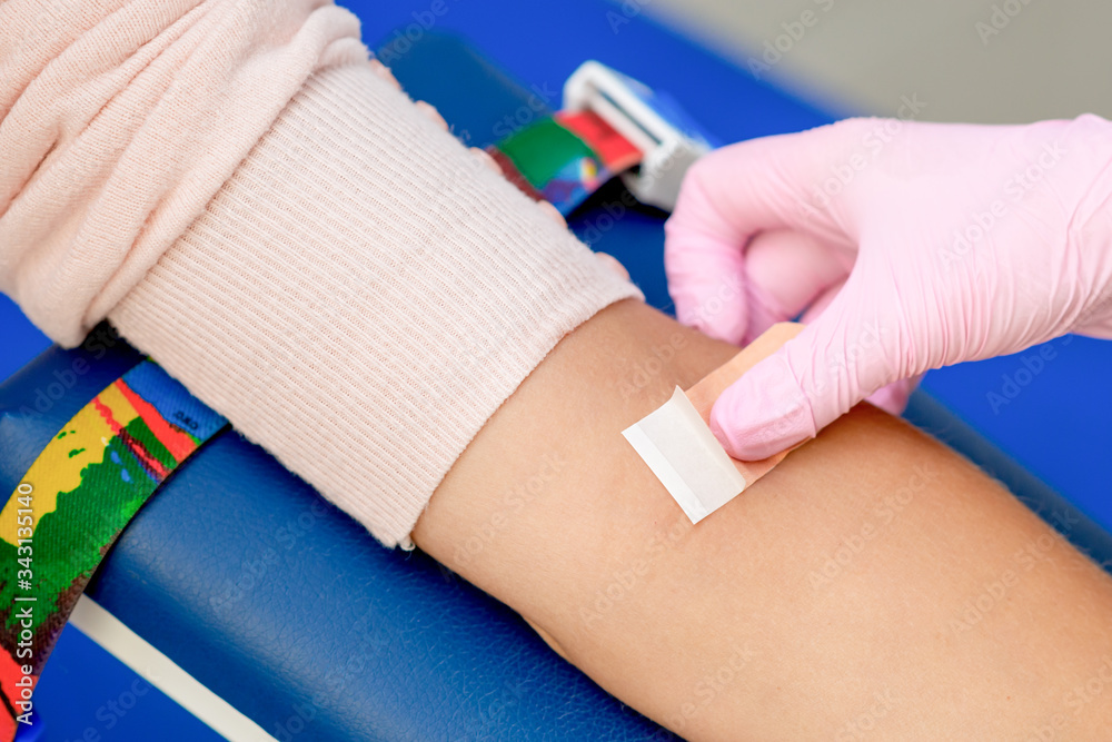Nurse hand is glueing an adhesive plaster on arm after blood sampling ...