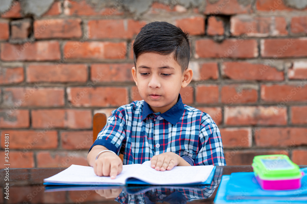 Primary school student in proper school uniform reading book on study ...