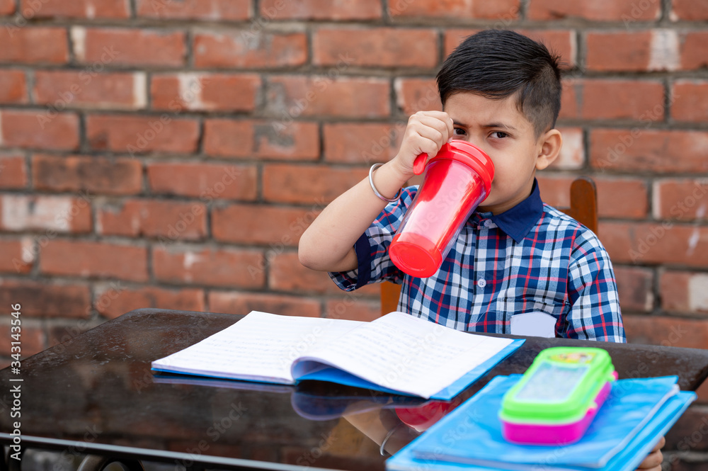 Primary school student drinking water with red water bottle while ...