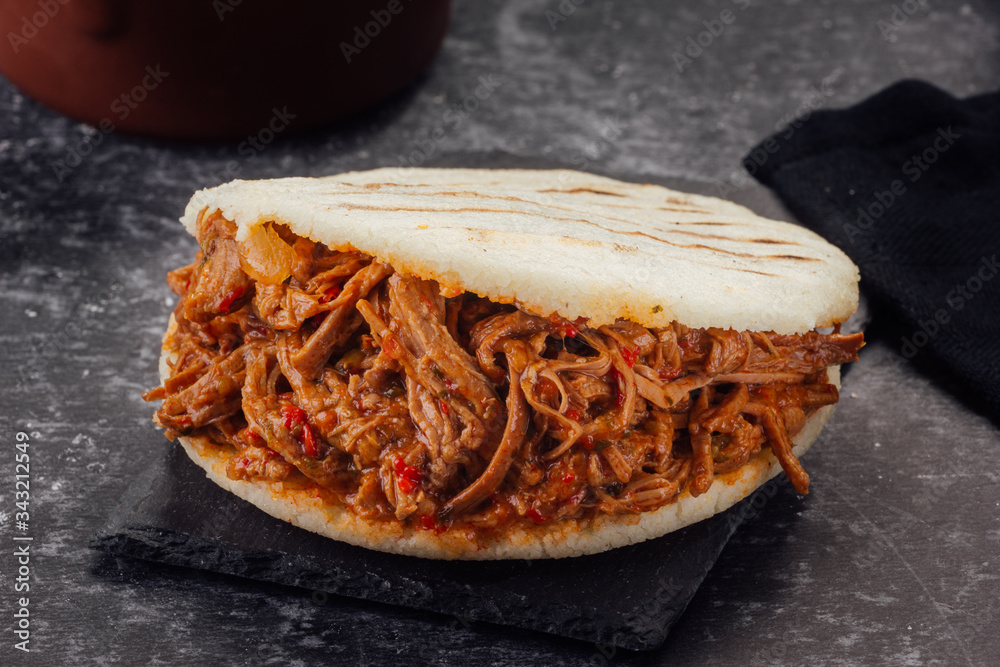 Arepa stuffed with shredded meat on a dark background. (Arepa con carne ...