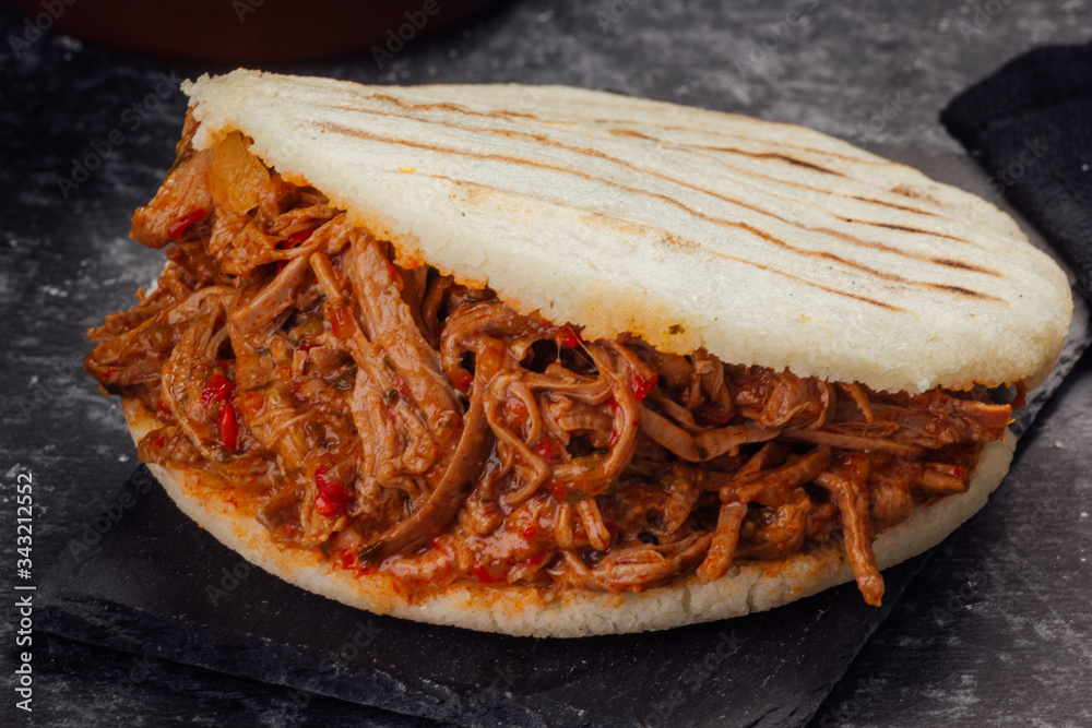 Arepa stuffed with shredded meat on a dark background. (Arepa con carne ...