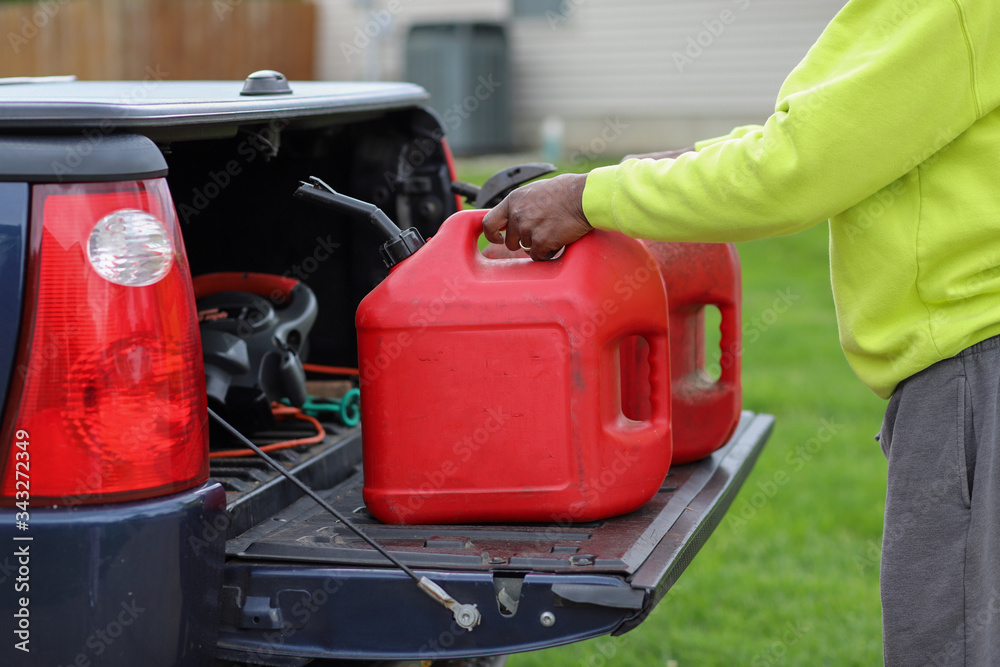 An African-American man holding two red plastic gas tank in a truck ...