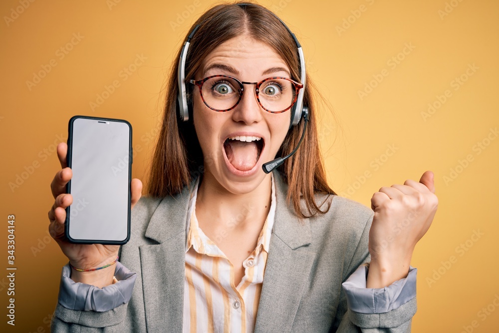 Young redhead call center agent woman using headset holding showing ...
