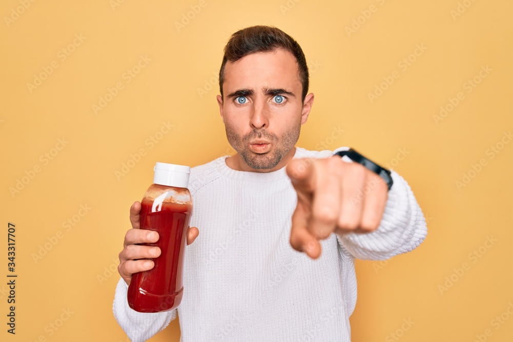 Young handsome man holding bottle of ketchup sauce condiment over ...