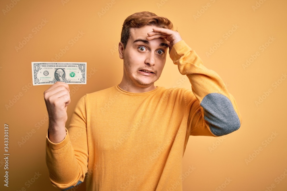 Young handsome redhead man holding one dollar banknotes over isolated ...