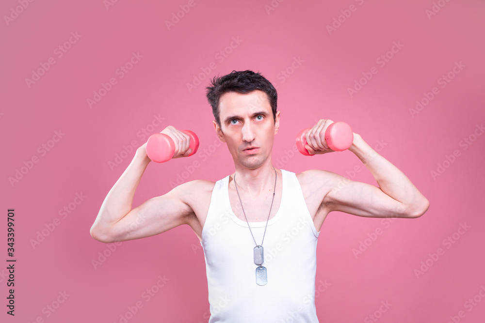 Skinny weak young man posing on camera with pink dumbbells. Exercising ...
