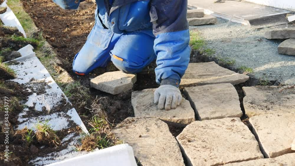 Hands hits a stone with a hammer to make it fit and to place stone ...