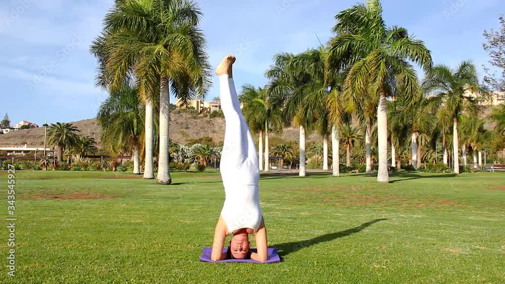 Young woman in parsva sirsasana on purple mat at green grass park on ...