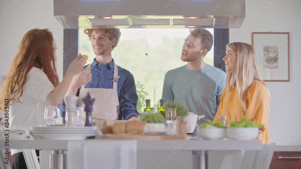Four people talking while cooking together at home in modern kitchen ...