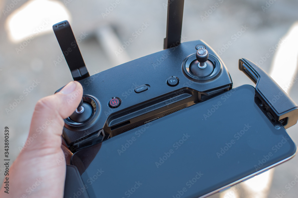 Hand holding drone remote controler to operate flying drone on a sunny ...