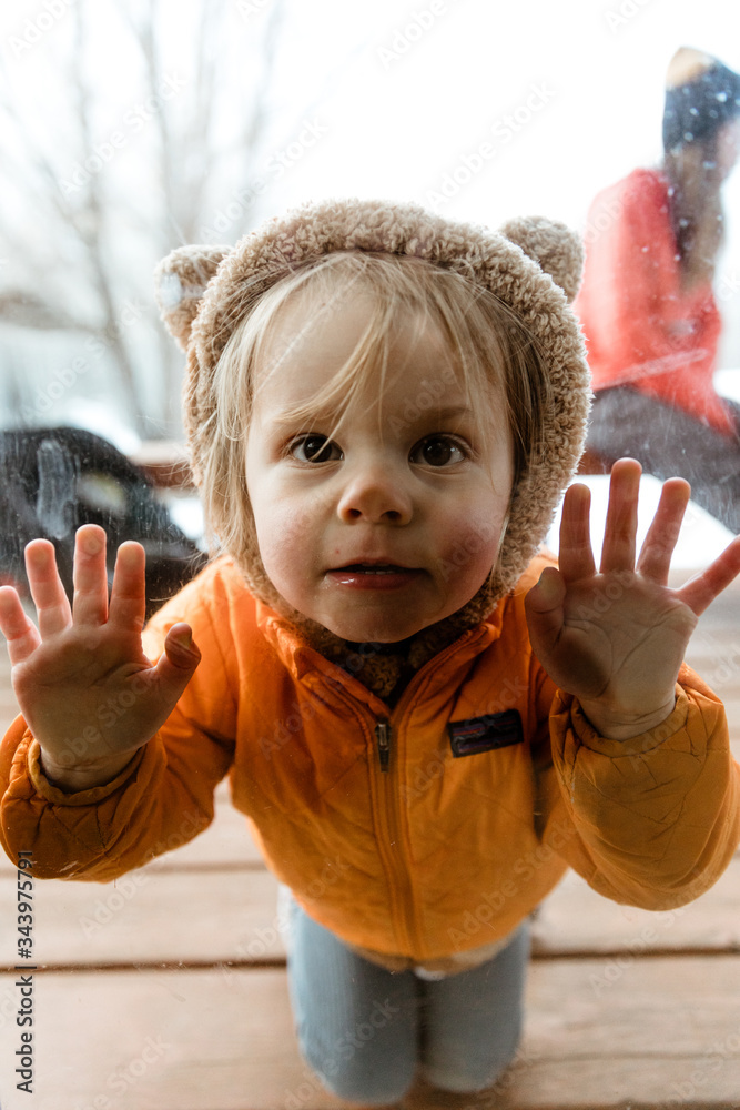 young blonde kid pushes face and hands against glass during quarantine ...