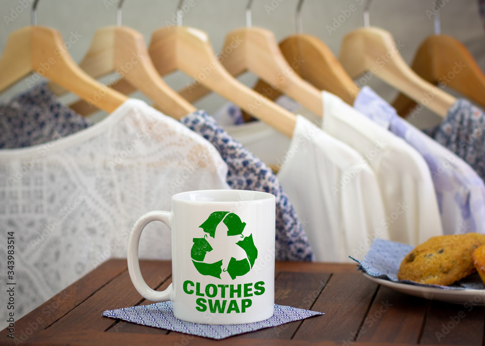 Clothes swap icon and text on mug in front of clothes at swap party ...