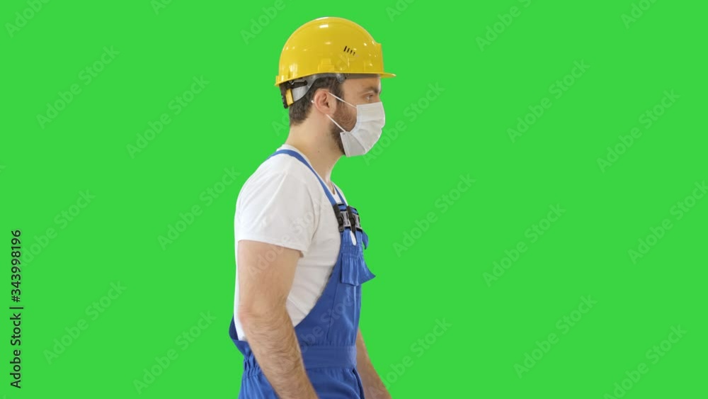 Construction worker wearing a hardhat and mask walking on a Green ...