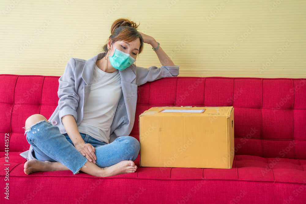 Beautiful Asian woman wearing a face mask is sitting on red sofa with ...