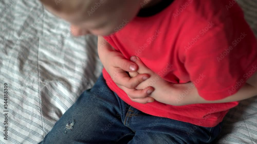 little boy is holding his hands to his stomach and writhing in pain ...