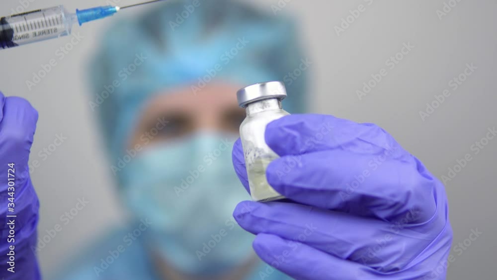 Doctor drawing up solution from vaccine bottle and filling syringe ...