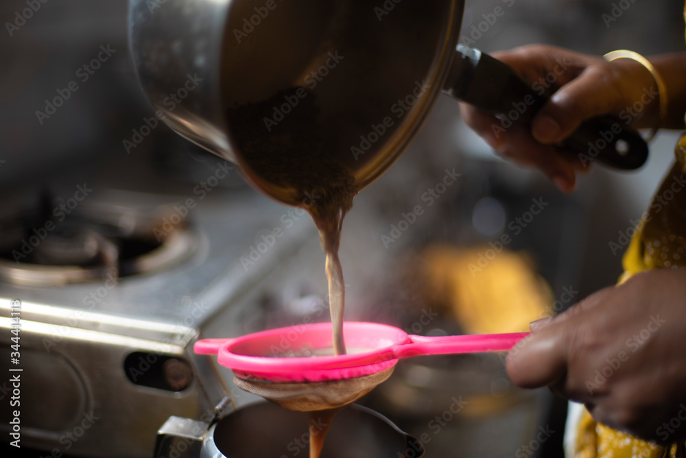 Tea being strained and poured into the cups from a steel tea pot in an ...