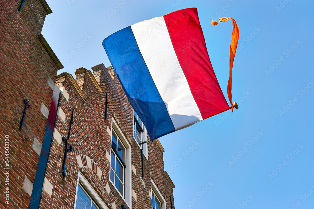 Dutch flag with orange streamer waving in the wind on the facade of a ...